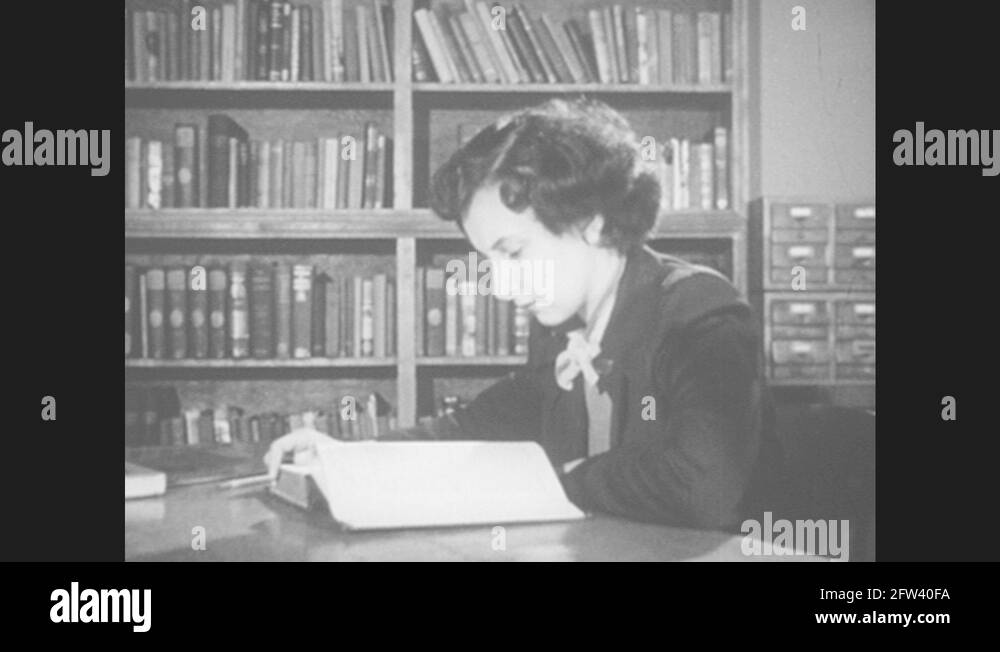 1950s: Teenage girl in library reads book. Page in book. While reading ...