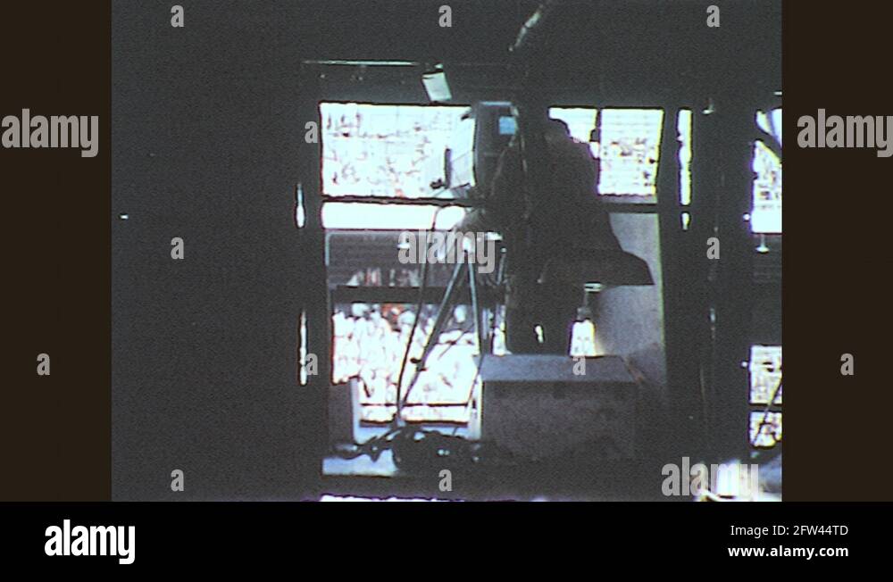 1970s: Man works TV camera from window. Men watch wall of screens. Two ...