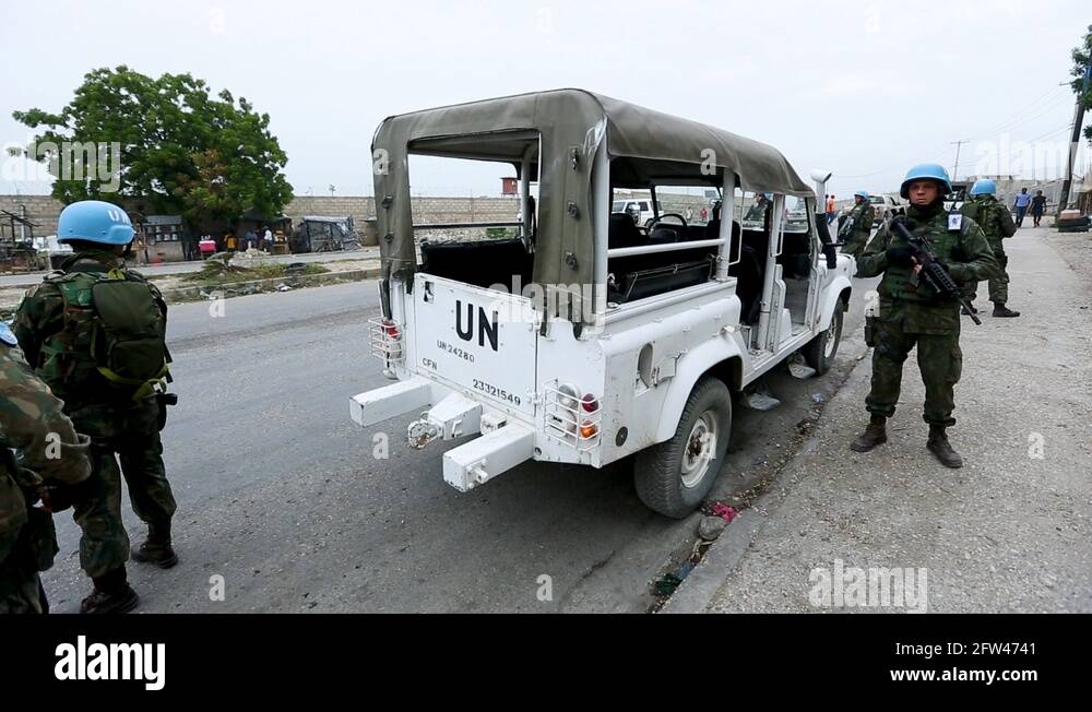 UN peacekeepers stand in formation around their vehicle near a busy ...