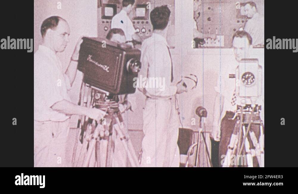 1930s: Man cranks camera, man directs men in TV studio. Men adjust ...
