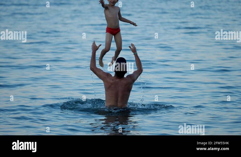 Father rising up child, kid jumping in sea water and show thumb up ...