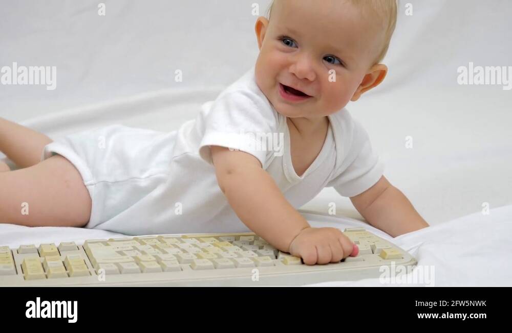 Little baby with blue eyes lying on his belly next a computer keyboard ...