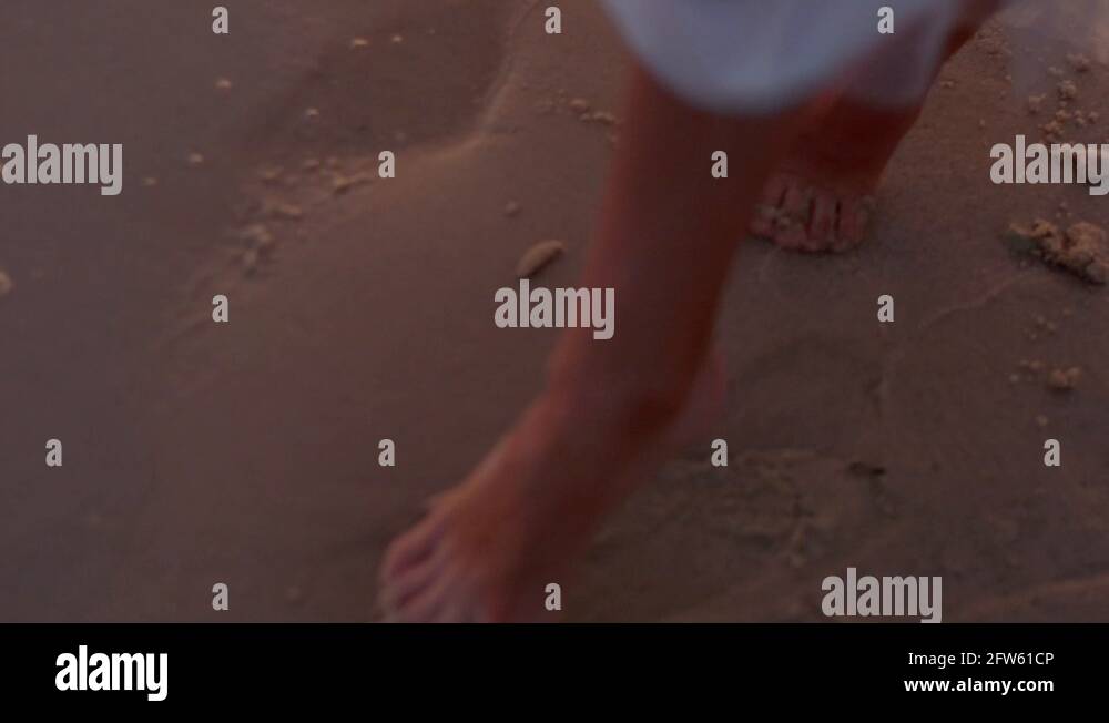 Woman walking on beach barefoot over sunset. Girl walking in shallow ...