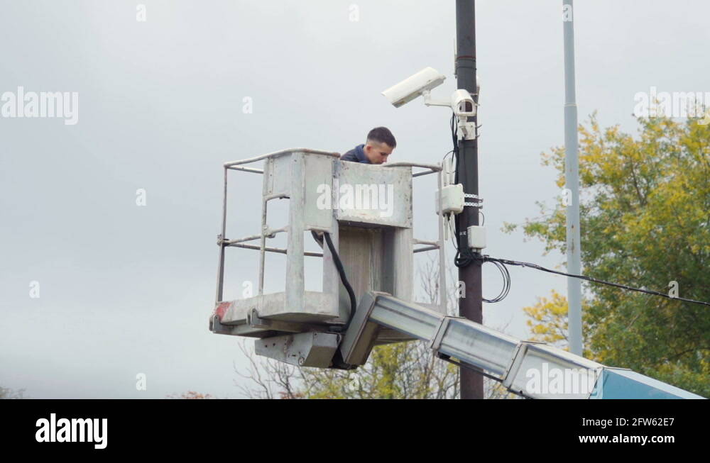 Electrician installs a video camera on a pole. Utility worker changing ...