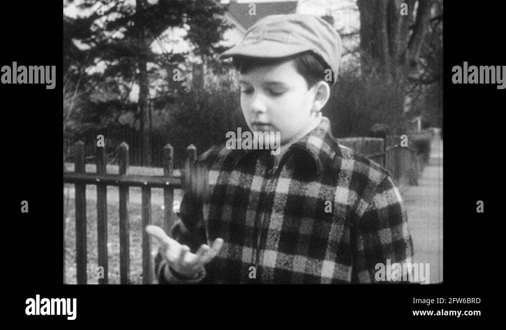 1940s: Young boy stands on street corner, throws rocks up and down in ...