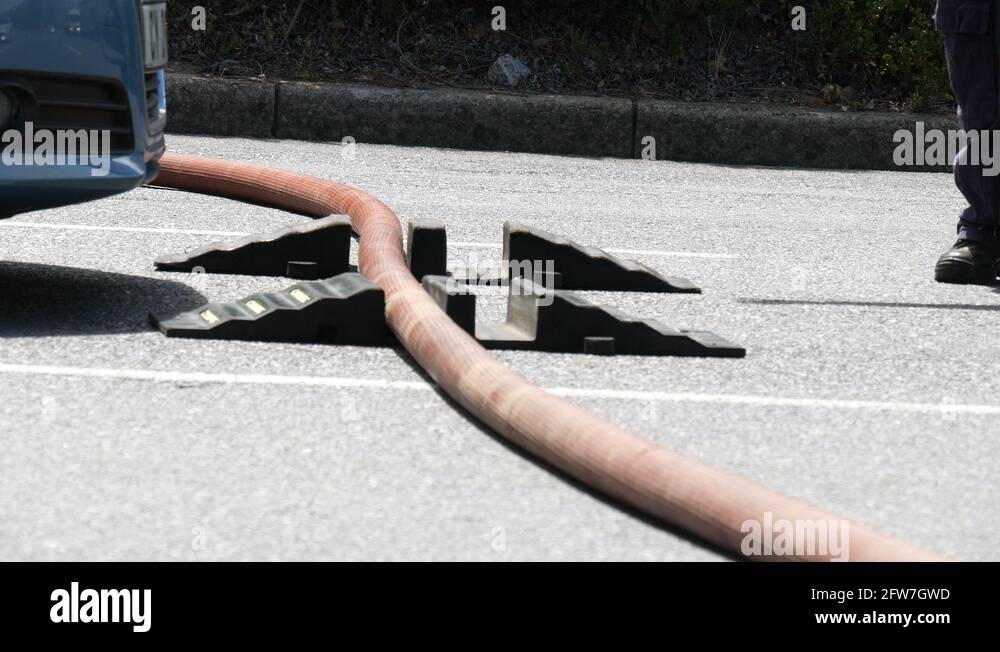 Vehicles drive across ramp over fire fighting hose with men's legs in ...