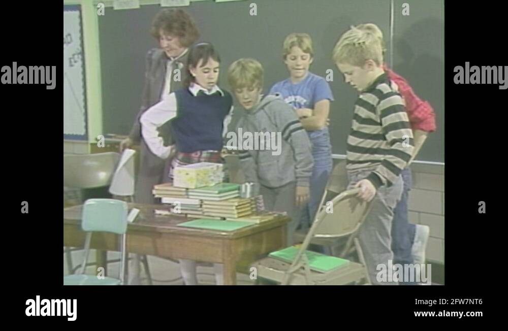 1980s: Kids in classroom play with slinky on stack of books on desk ...