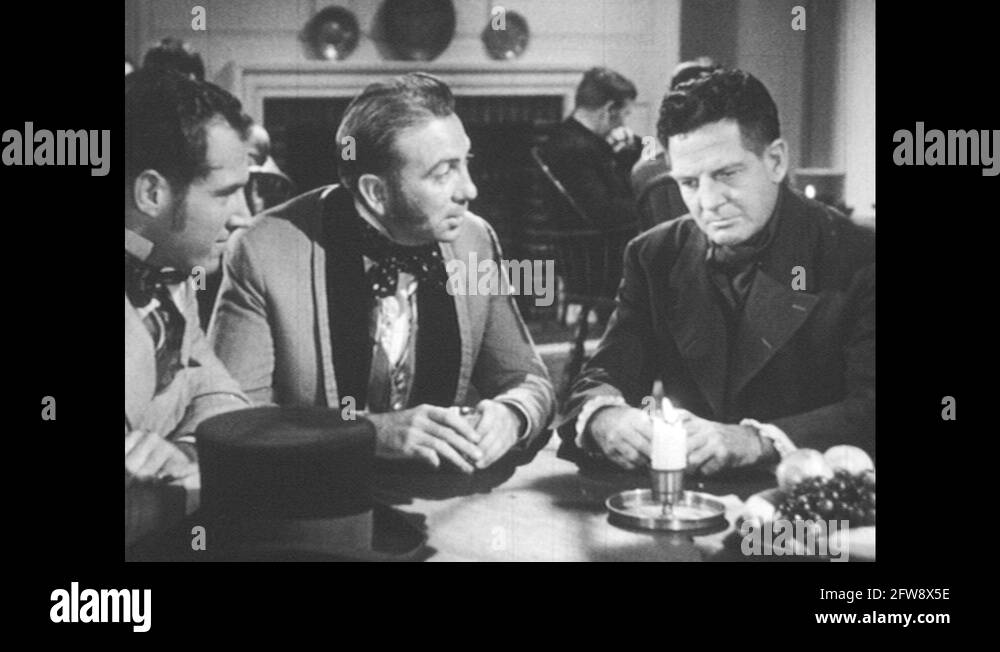 1950s: Three men in 19th century clothes sit around table talking. One ...