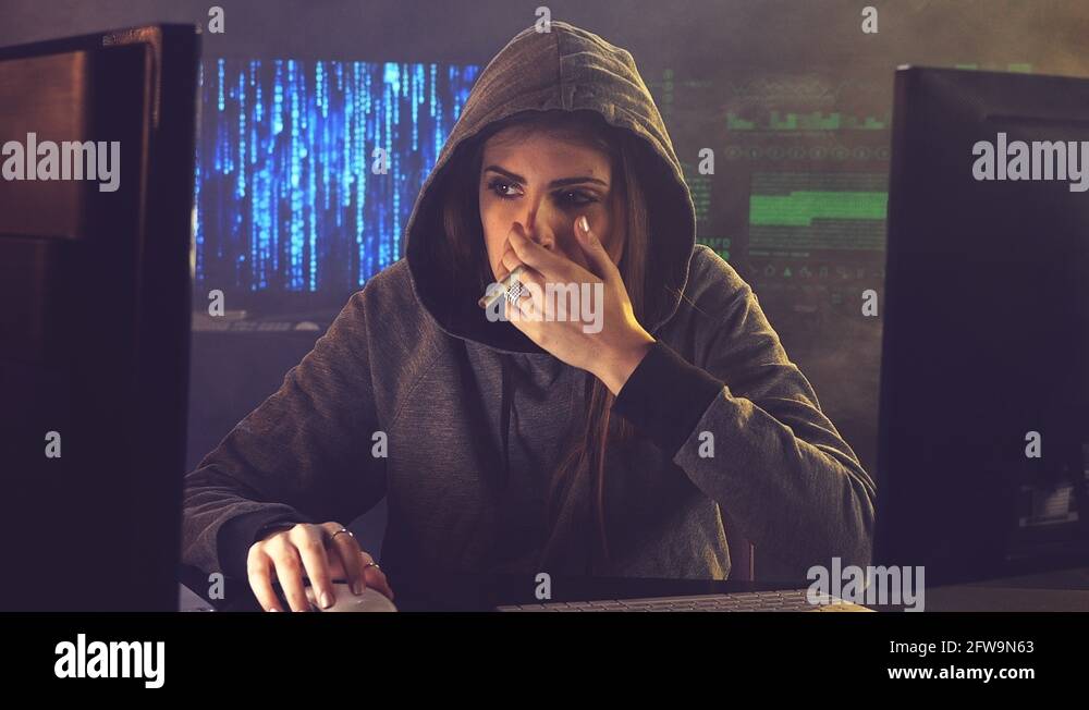 Female programmer hacker with hood working at night in front of screens ...