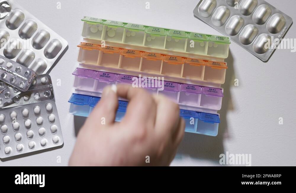 Weekly dose pill organizer. Man's hand puts medication into a pill ...