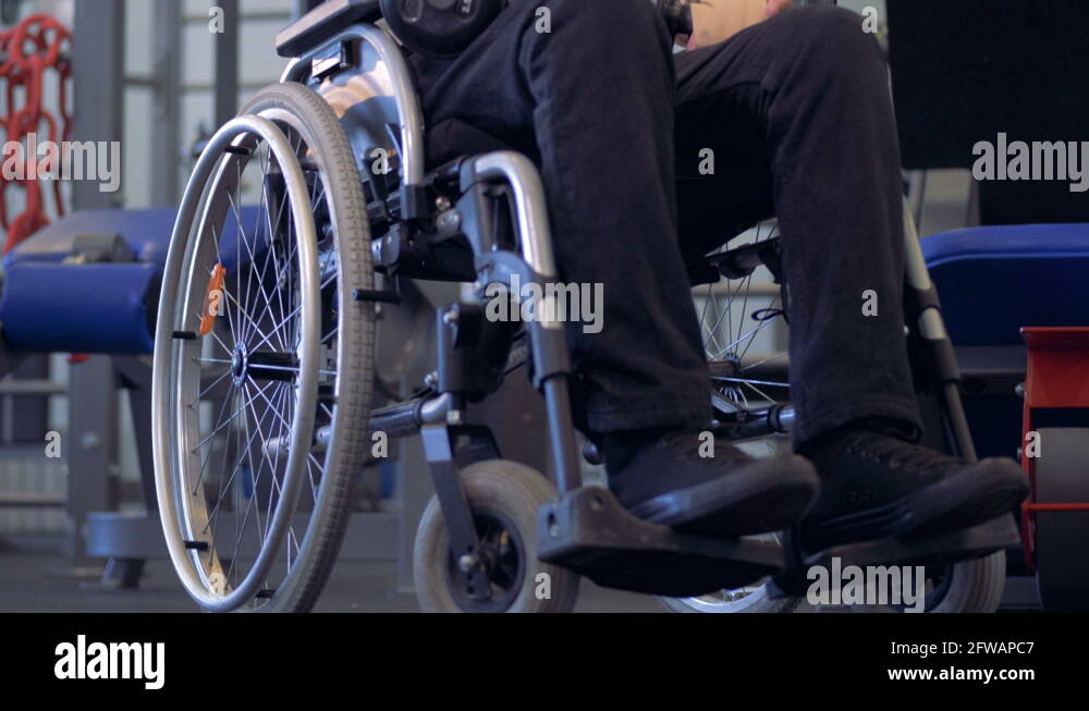 A disabled man is sitting in a wheelchair with dumb-bells, moving his ...