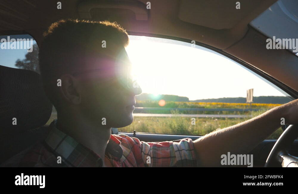 Profile of young man in sunglasses driving a car with sun flare at ...