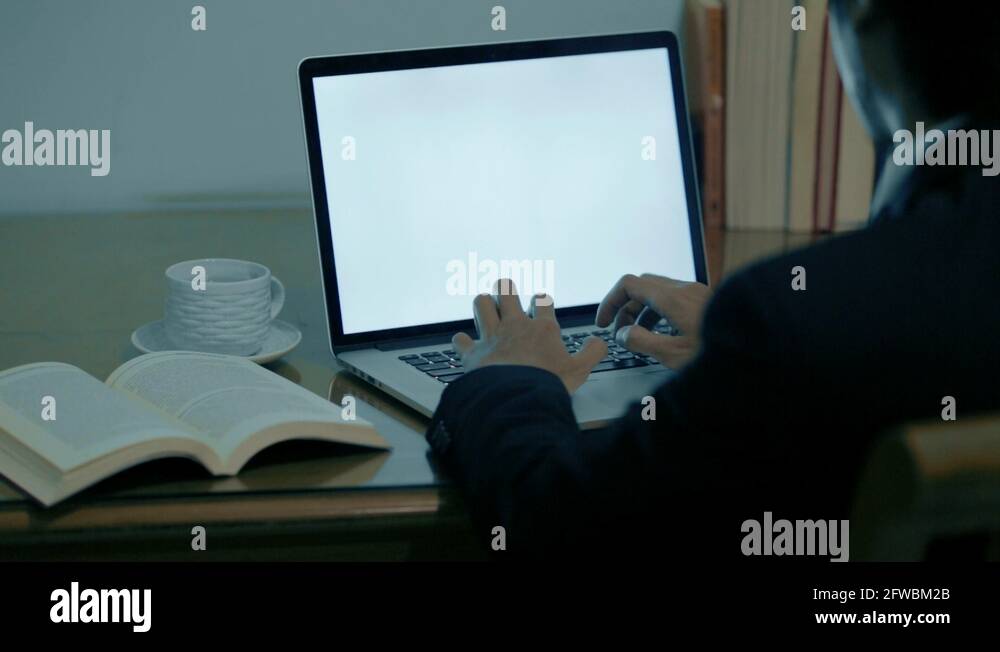 Back view of a man sitting at his desk and typing on a laptop with ...