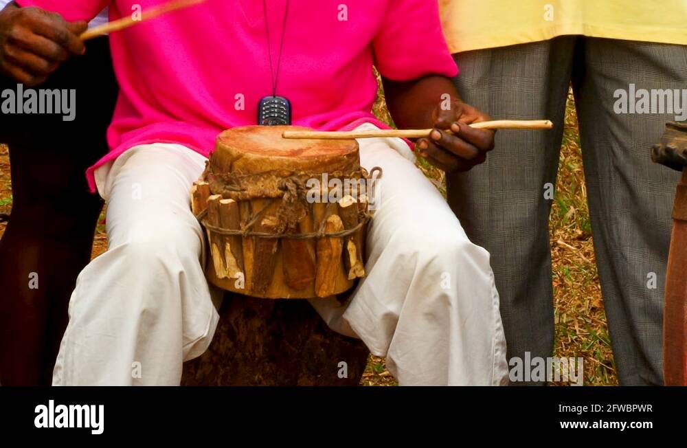 African man plays a homemade bongo drum with makeshift drumsticks in a ...
