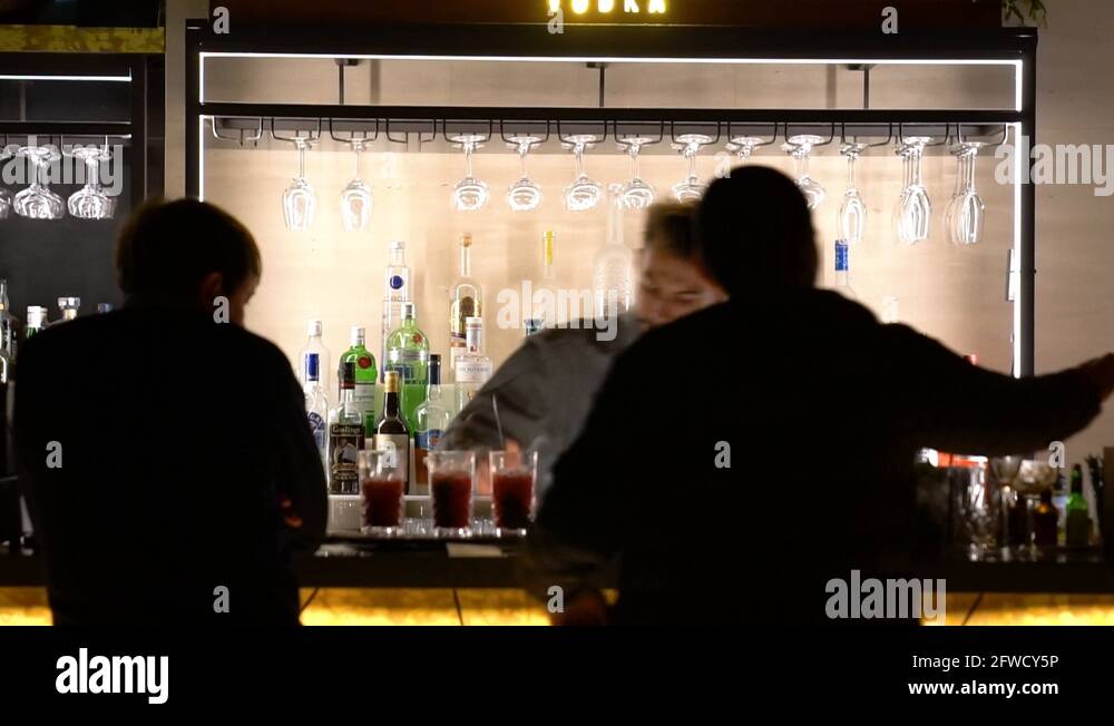 Bartender mixing drinks in a classy bar and customers coming over to ...
