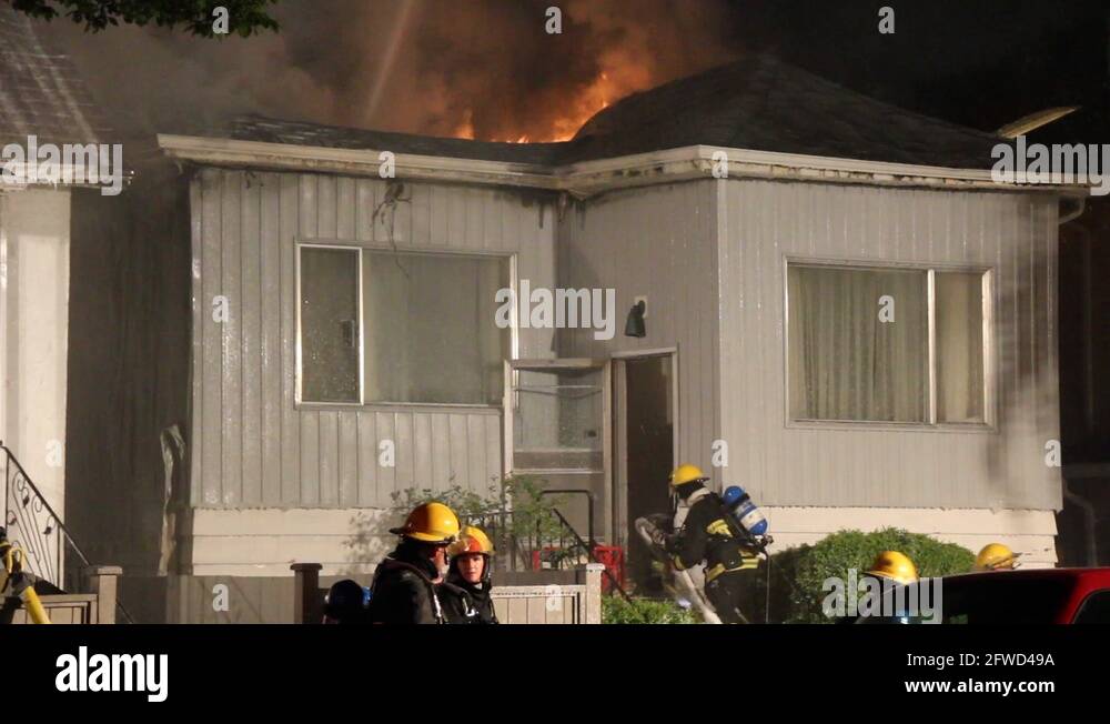 Fireman pulling hose into a single story house ablaze in the evening ...