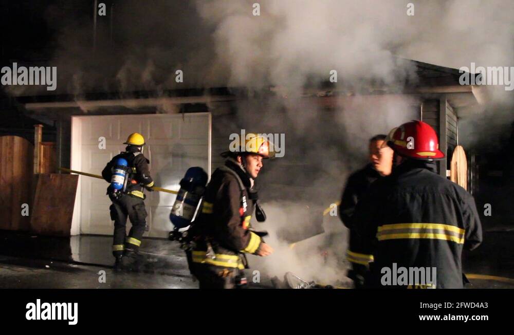Proximity view of multiple firemen operating at garage fire in back ...