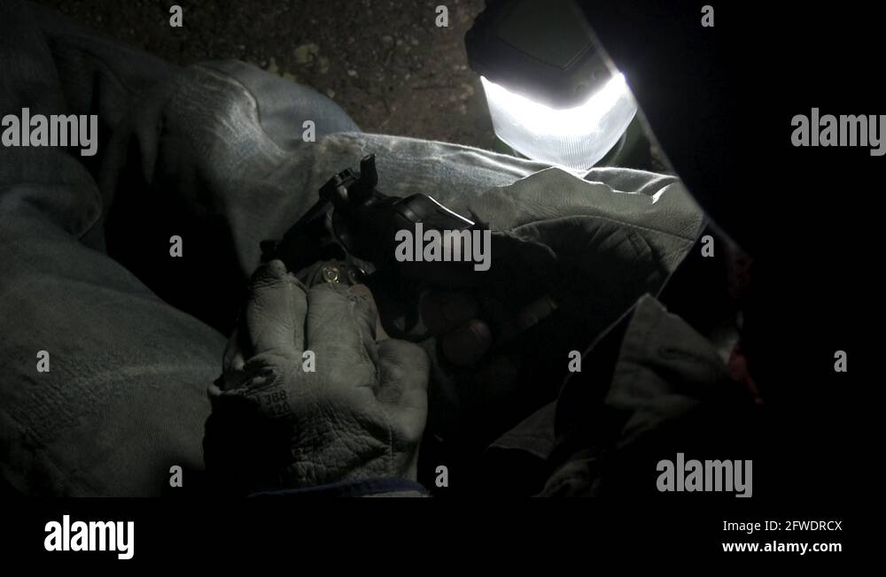 Over the shoulder hooded man loading handgun in woods, static nighttime ...
