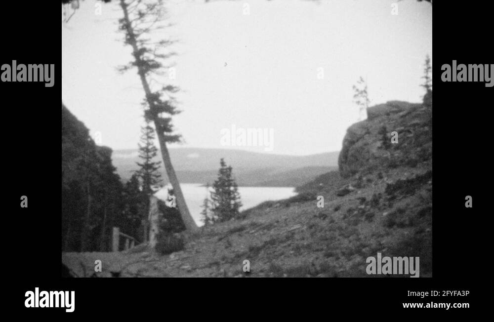 1920s: Mountain lake vista. People board boat docked at lake. People ...