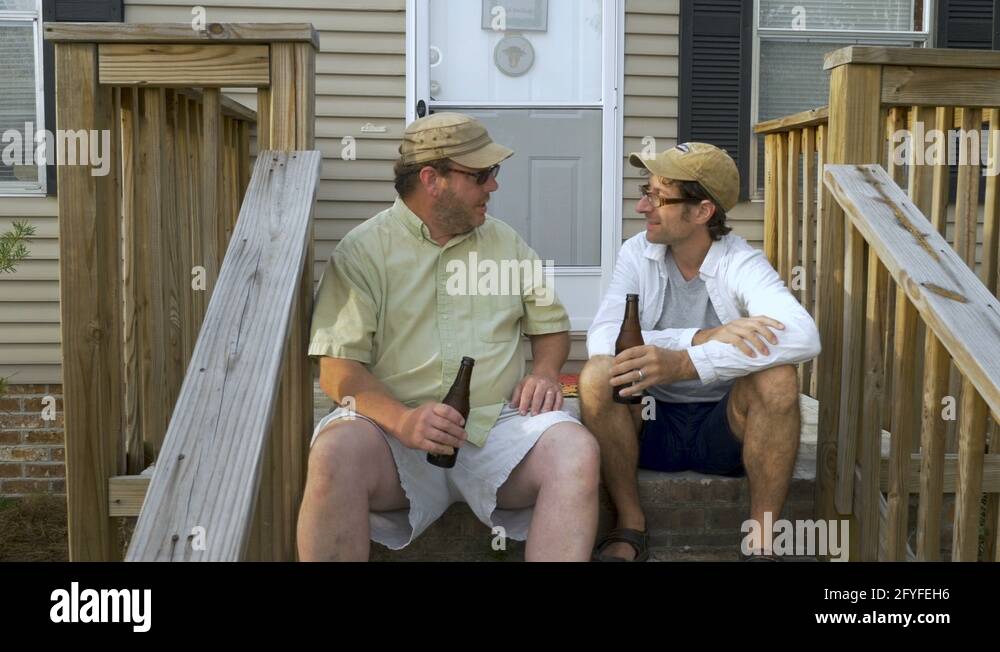 Two men sitting on porch steps talking, holding drinks and relaxing ...