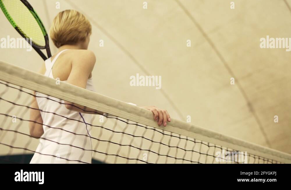 Backside footage of girl walking with racket, touching the net with the ...