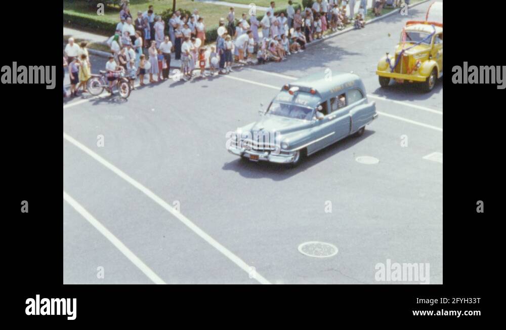 1950's: Gray ambulance, floats, tow trucks move along street in parade ...