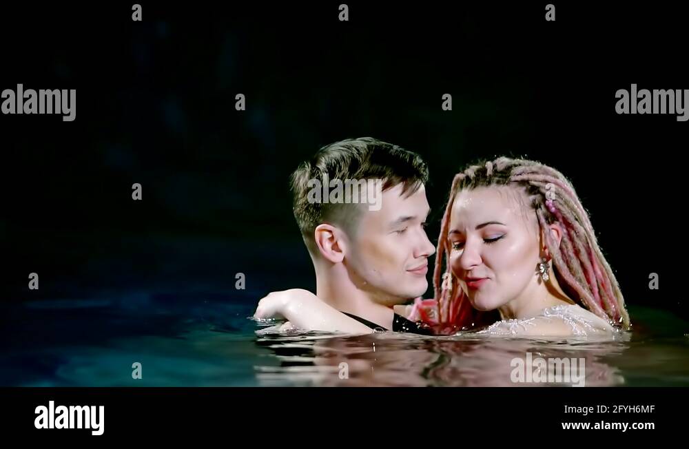 pair of lovers is floating in dark pool, young woman with dreadlocks is ...