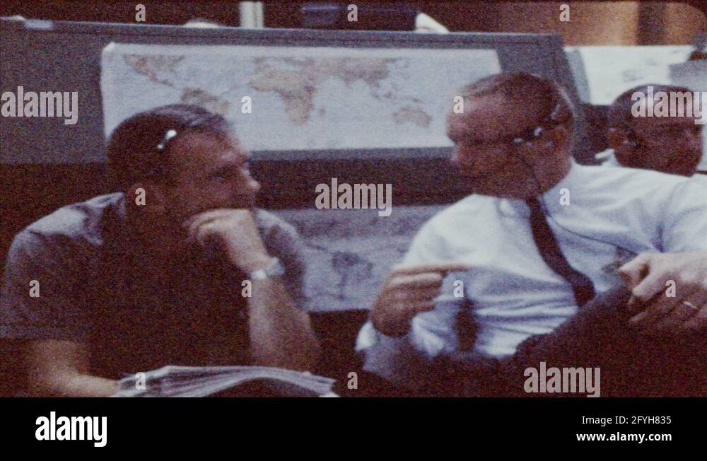 1960s: Neil Armstrong talking to man. Men seated at control panel, zoom ...