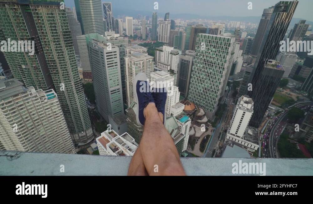 Young man sitting on the edge of roof of skyscraper, he sees his feet ...