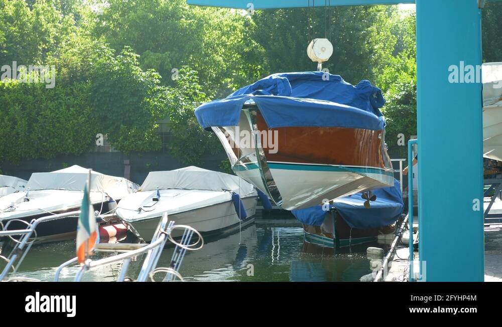 A classic luxury wooden runabout boat lowered with a crane in a marina ...