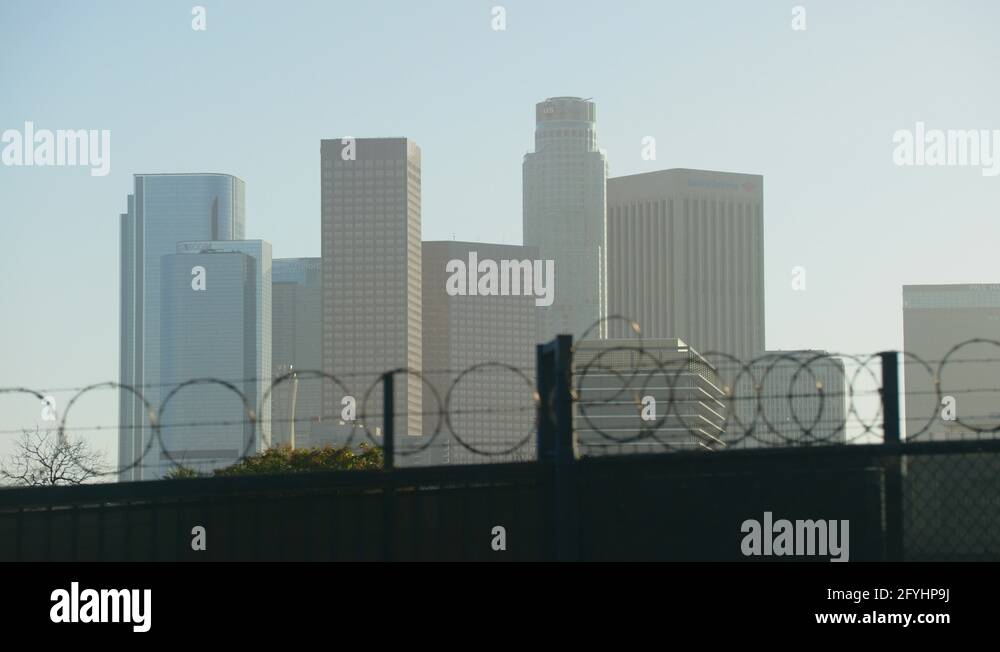 Skyscrapers of Los Angeles seen behind a barb wire sliding gate ...
