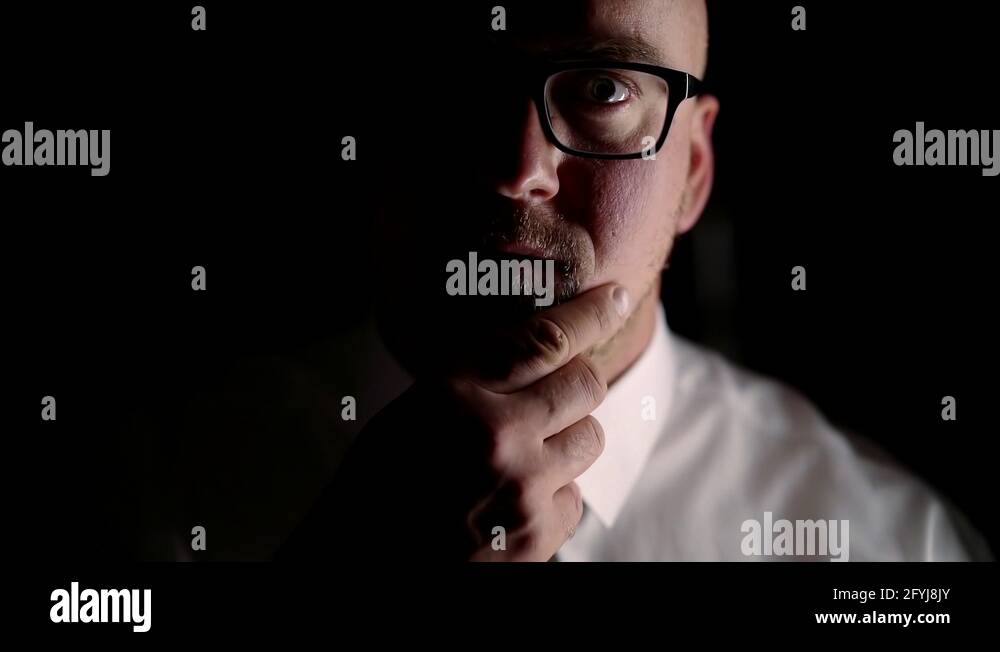 Portrait of sad man in dark room with hard light. Wearing a white shirt ...