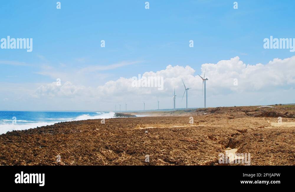 Wind turbines spinning along rocky beach with ocean waves in Curacao ...