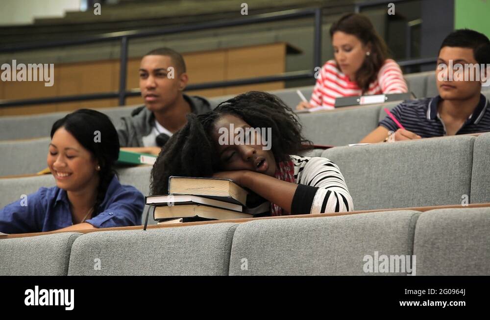 Female student falling asleep on books in lecture theatre, during class ...