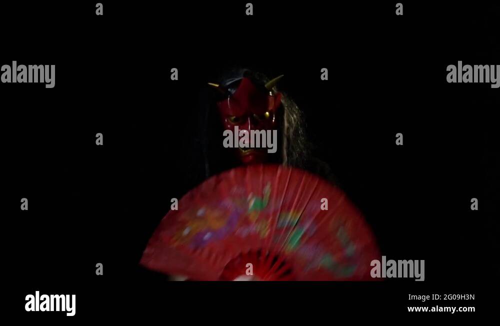 A freak in a mask of a Japanese demon with long hair come ous from ...