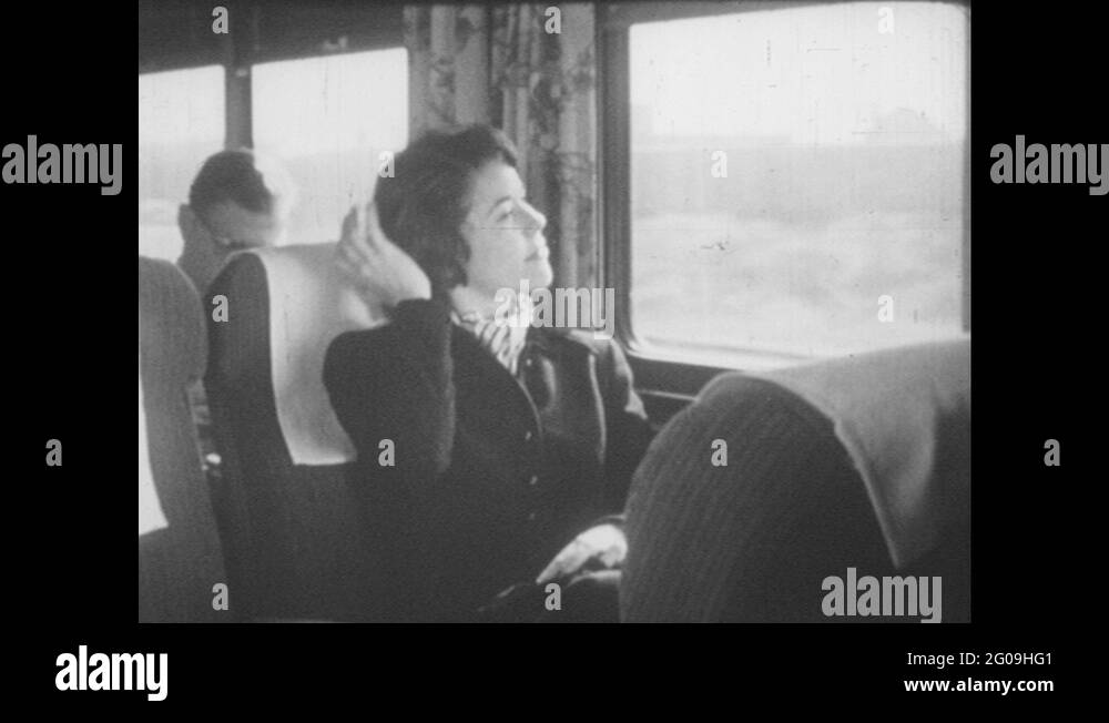 1950s: Woman seated on train touches her hair. Man, woman and cab ...