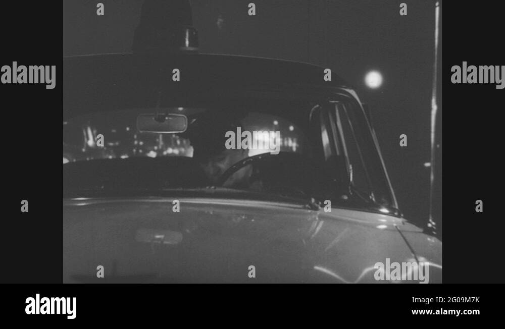 1950s: Police officer talks on radio in police car at night. Car speeds ...
