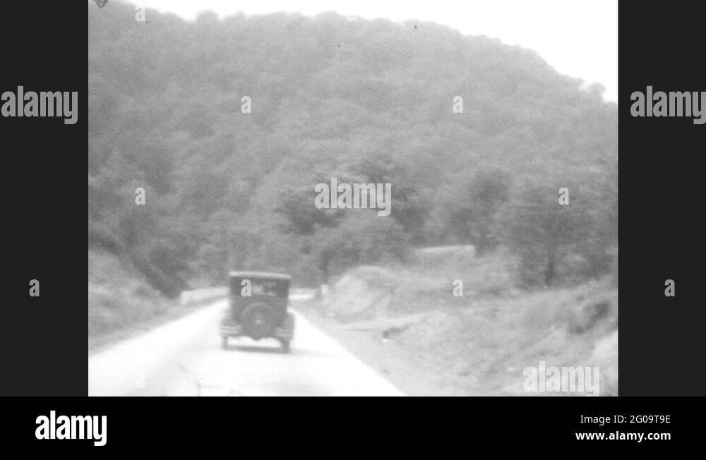 1920s: Vehicle driving along two-lane road in the mountains, closely ...