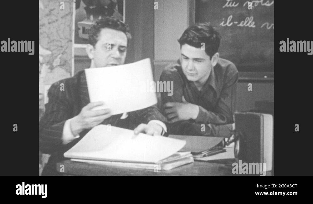 1950s: Teacher and student look at paper together. Man puts paper away ...