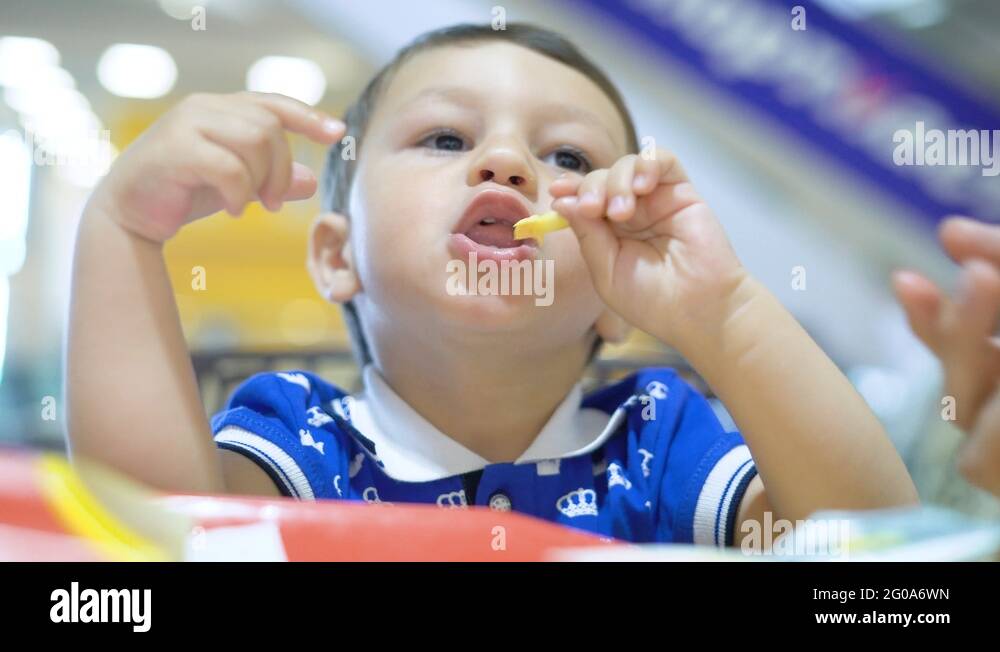 little cute boy eating hot french fries with his family in mall's cafe ...
