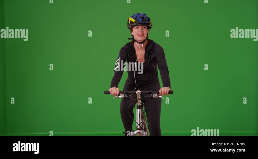Woman riding her bicycle toward the camera with a helmet on green ...