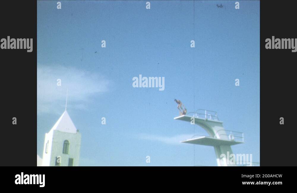1940s: Long shot, men posing on diving platform. Men dive into pool ...