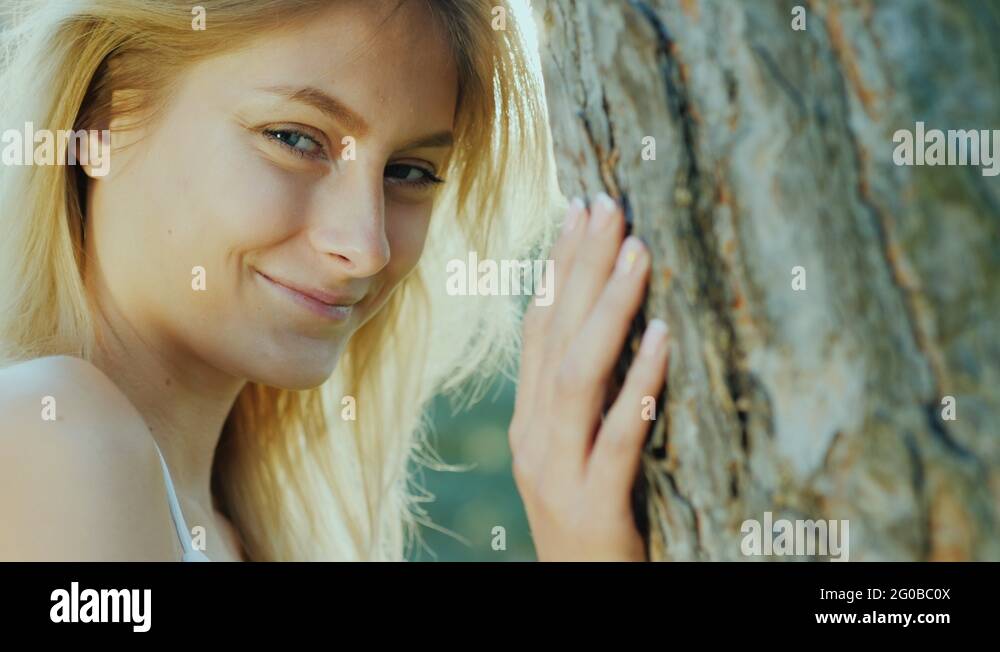 Beautiful young woman stands near a tree, portrait. Looks at the camera ...