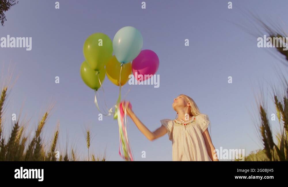 Child spinning with balloons at wheat field . Girl looking at camera ...