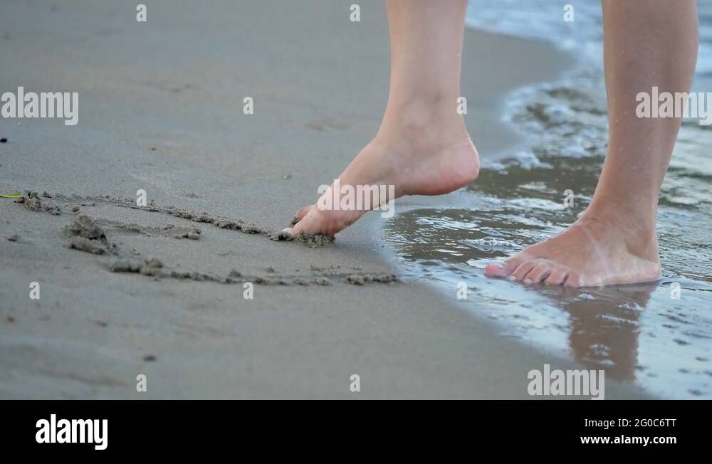 Woman feet drawing a heart on seashore, sea waves coming and remove the ...