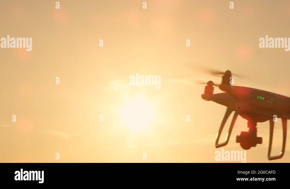 SLOW MOTION CLOSE UP LENS FLARE: Small filming drone flying on golden ...
