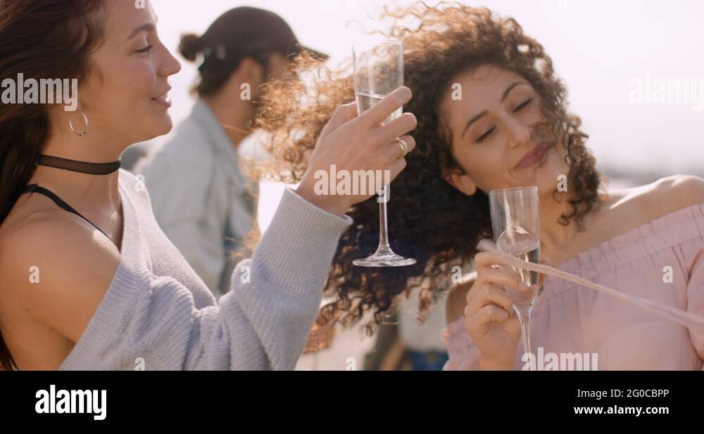 Two young women dancing back to back, with glasses in their hands and ...