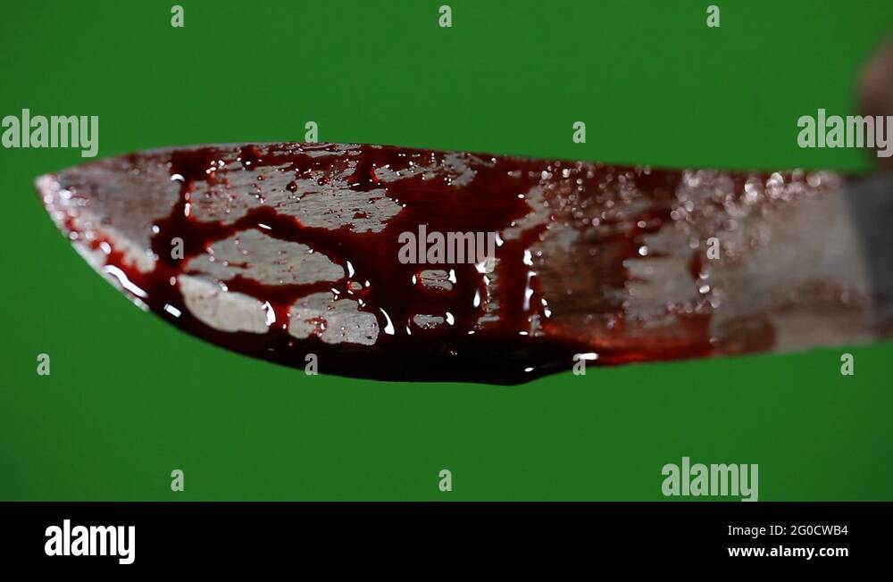 Close-up of a bloody knife blade being twisted in front of a green ...
