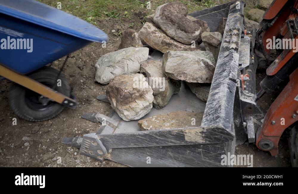 Large rocks are dumped from a wheelbarrow into the large bucket of a ...