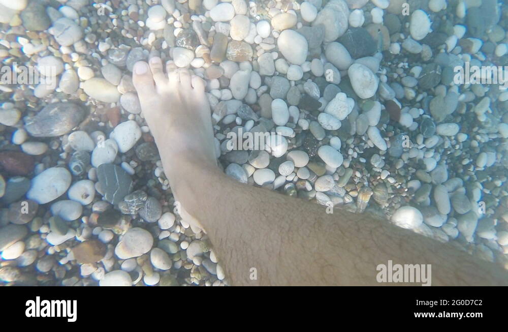 Little fish bites male leg. Feet of man stand in water on bottom of sea ...